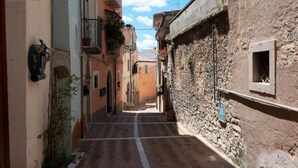 Rua estreita com edifícios de ambos os lados, alguns com varandas e plantas.