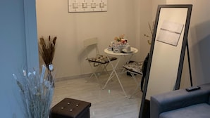 Uma sala de estar moderna com um sofá cinzento, uma mesinha redonda com um vaso de flores, uma cadeira e um quadro emoldurado encostado na parede.