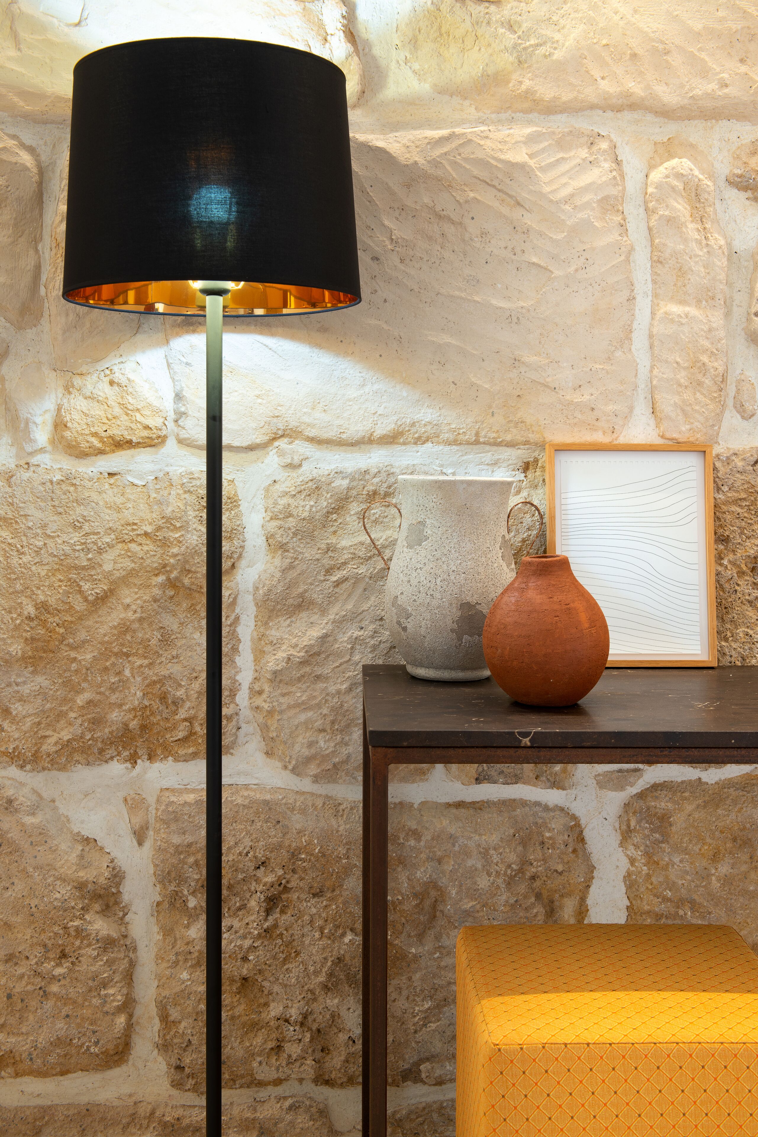 Um candeeiro, um vaso e um quadro emoldurado sobre uma mesa, em frente a uma parede de pedra.
