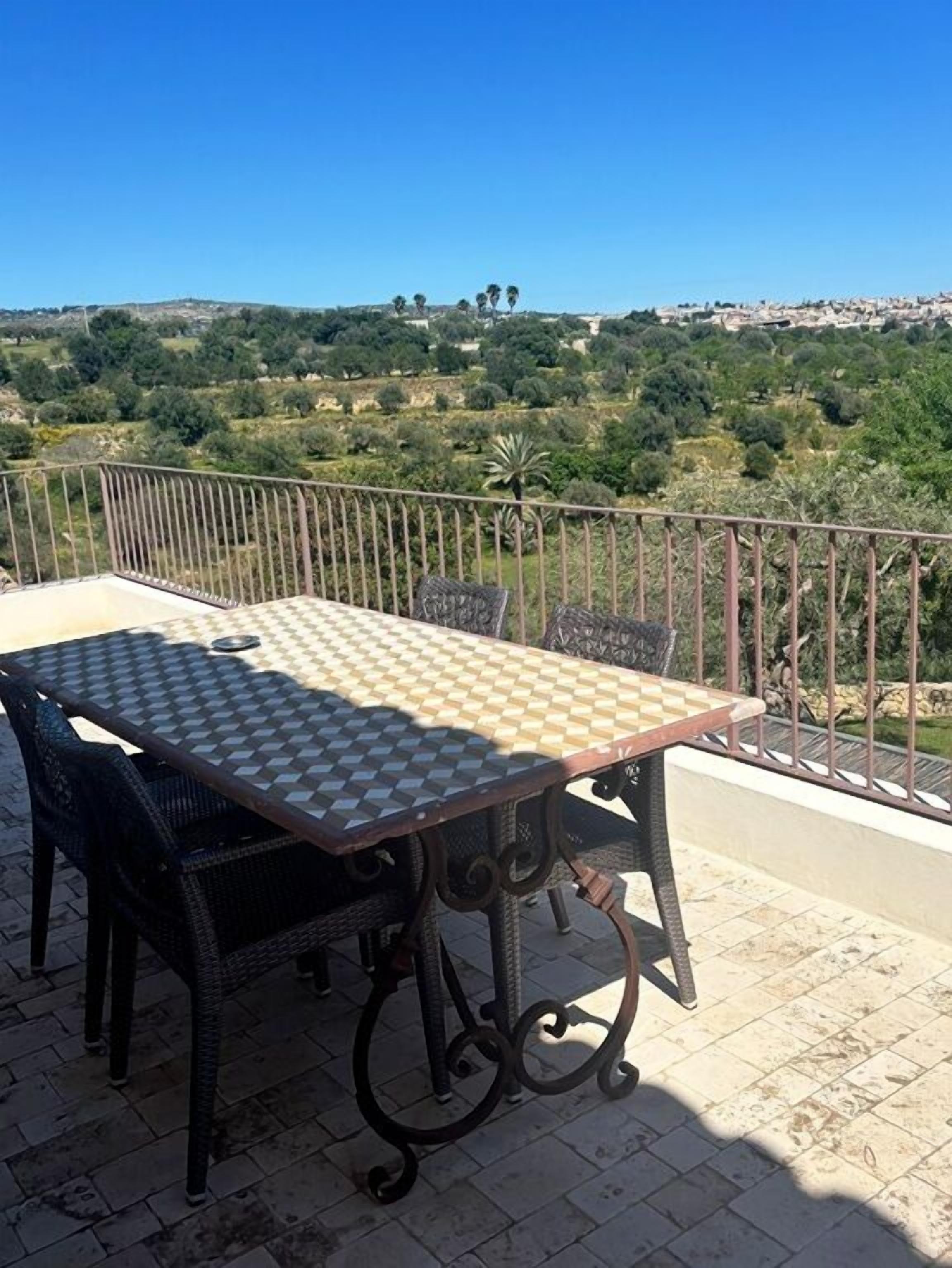 Mesa com cadeiras numa varanda com vista para uma paisagem deslumbrante.