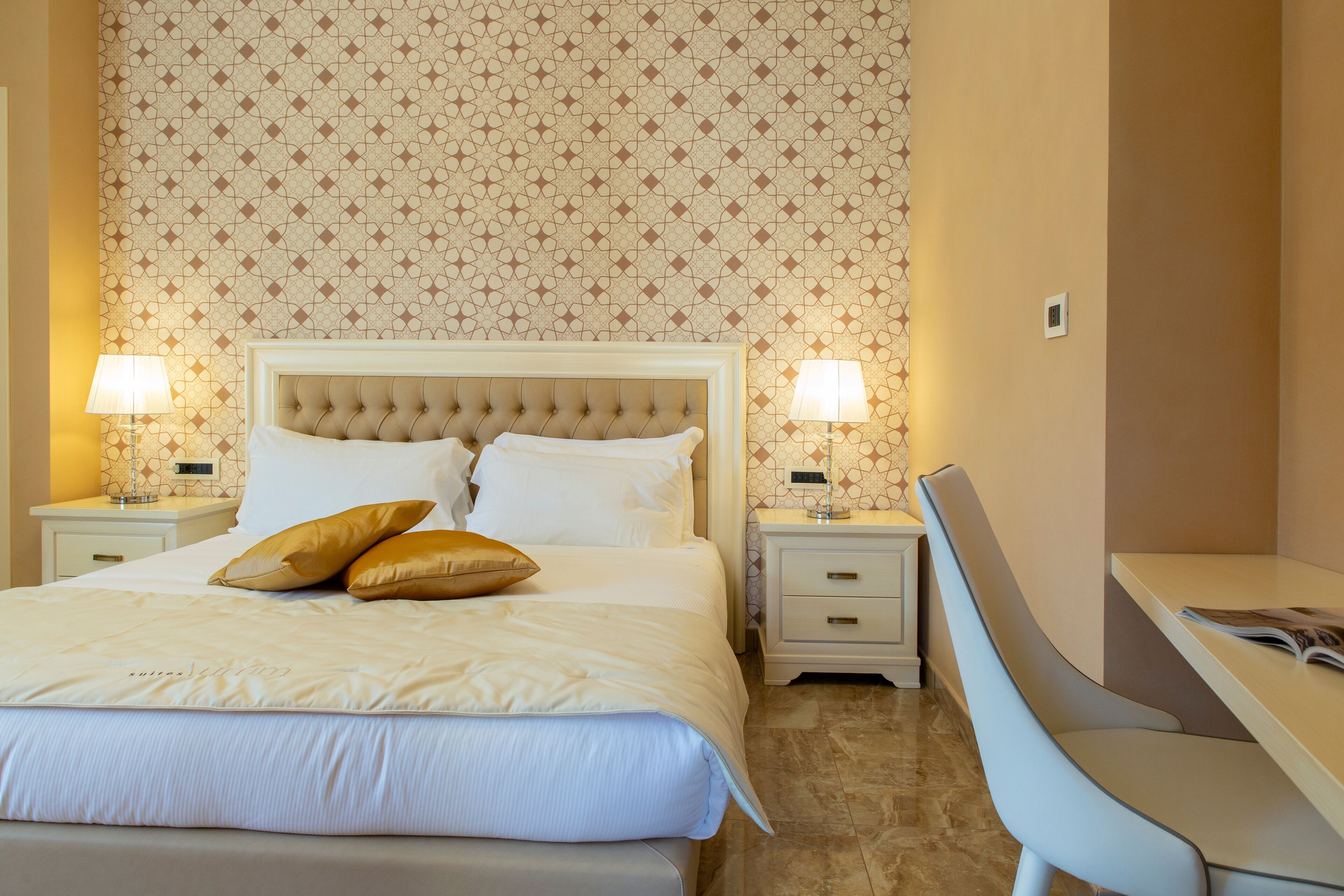 Quarto de hotel com uma cama grande, duas mesas de cabeceira com luminárias, uma escrivaninha e uma cadeira.