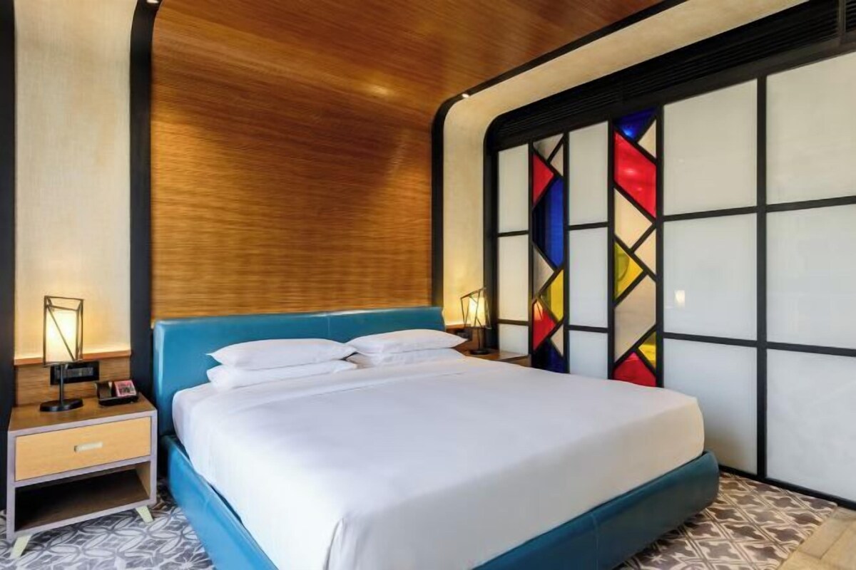 Quarto de hotel moderno com uma cama grande, teto de madeira e uma janela de vitrais colorida.