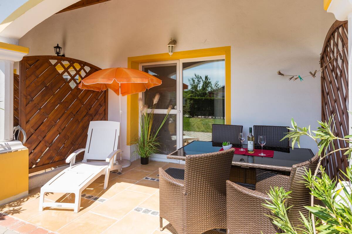 Um pátio com móveis de vime, uma mesa de vidro e um guarda-sol laranja.