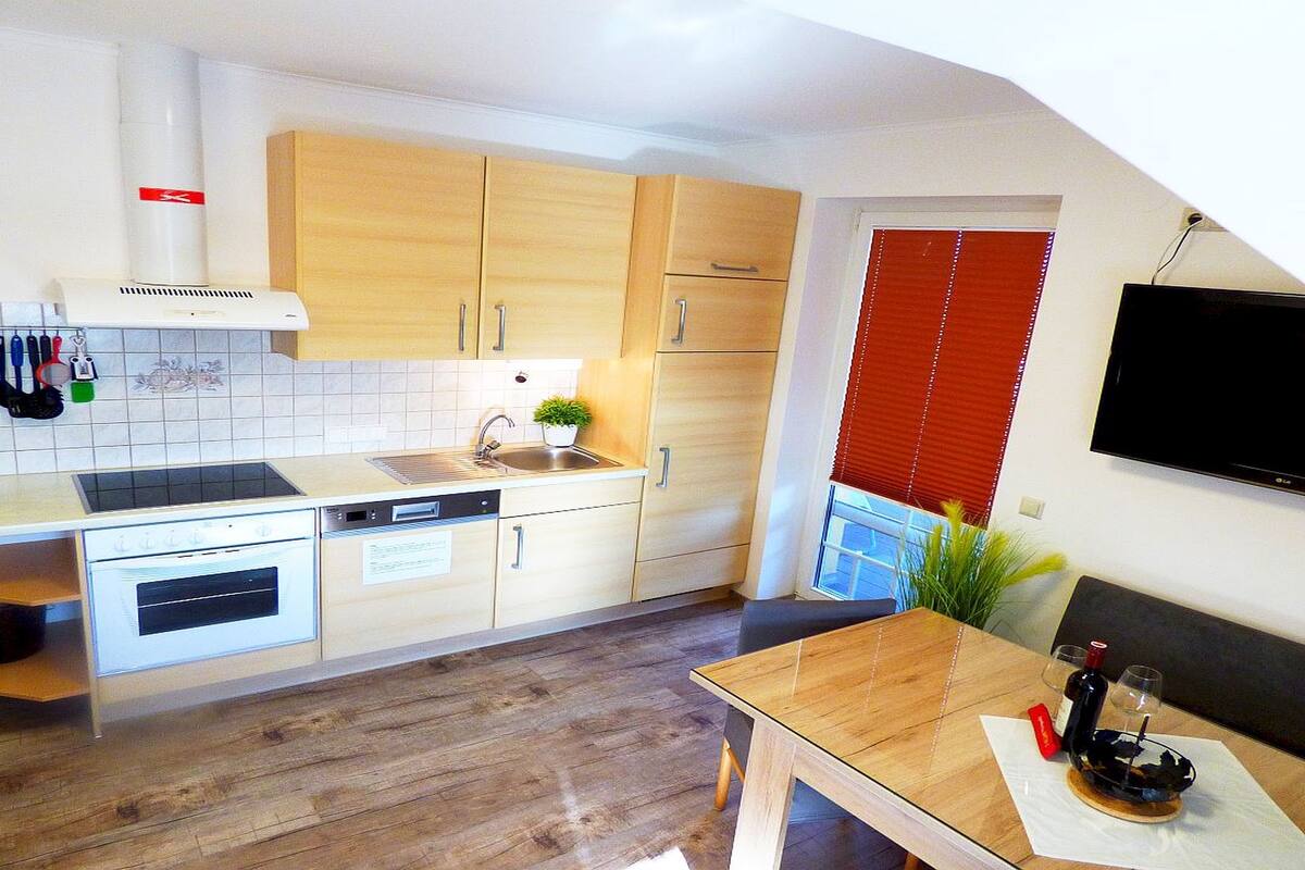 Uma cozinha compacta com eletrodomésticos modernos, área de jantar com mesa e uma TV fixada na parede.