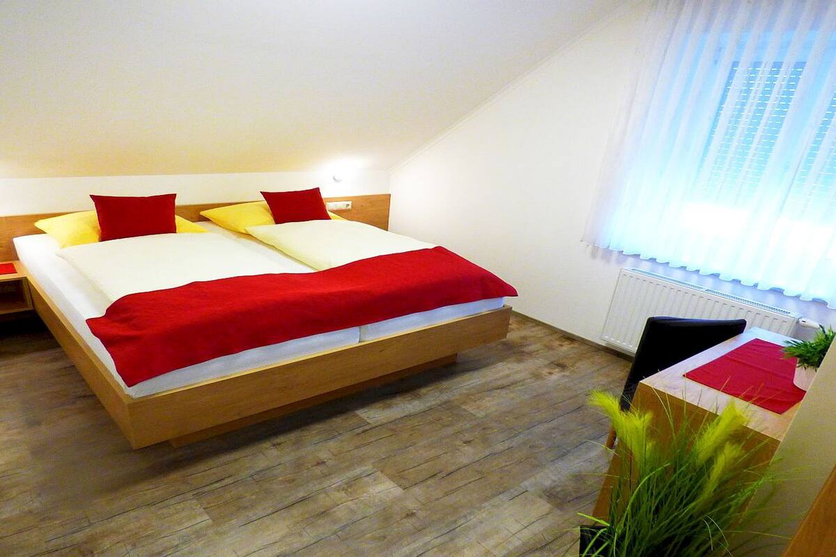 Quarto com cama, mesa de cabeceira e janela com cortinas.