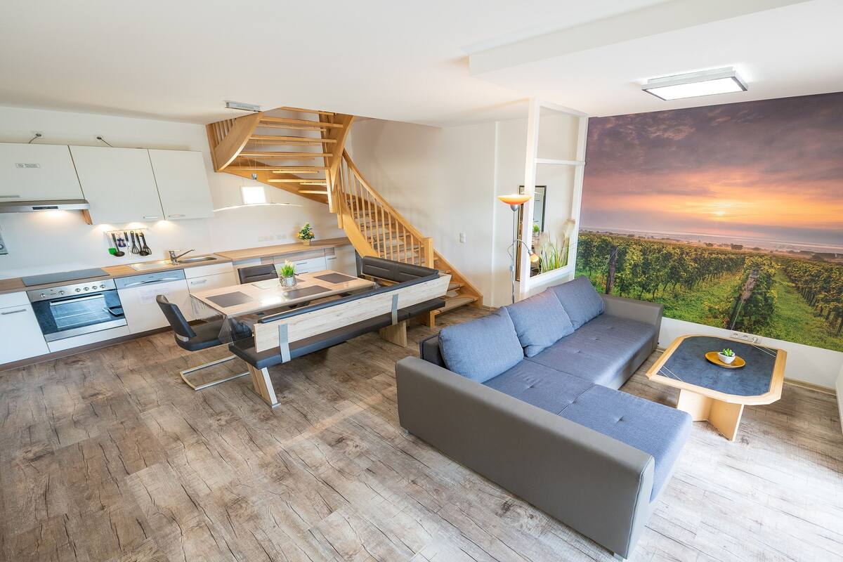 Um apartamento moderno com cozinha, área de refeições e sala de estar com uma grande janela com vista para um vinhedo.