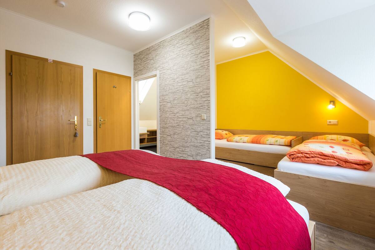 Quarto com duas camas, portas de madeira, parede de pedra e parede amarela com luminária.