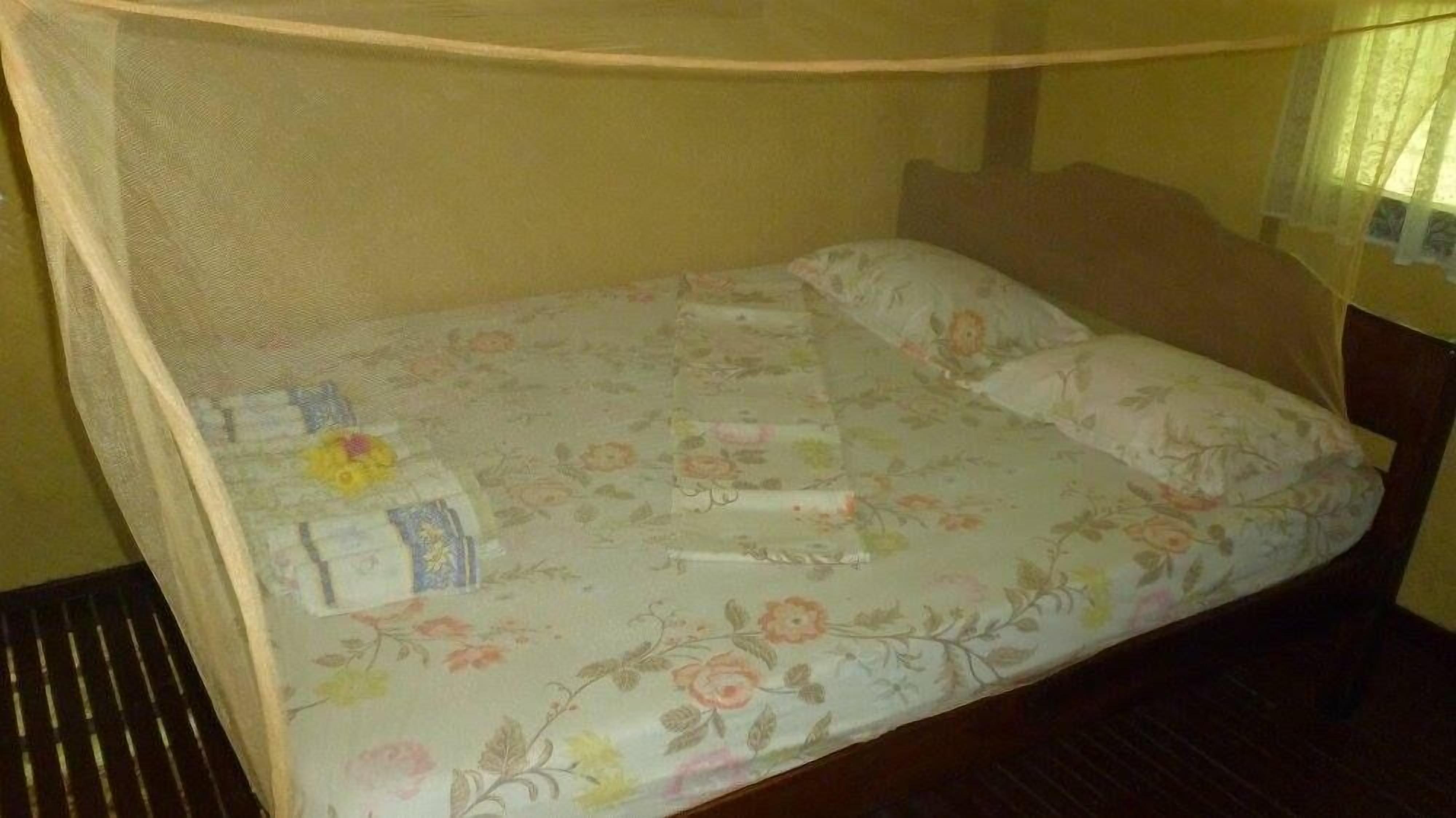 Uma cama de solteiro com colcha floral, mosquiteiro e cabeceira de madeira.