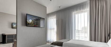 Quarto de hotel com duas camas, uma televisão de tela plana na parede e janelas amplas com cortinas.