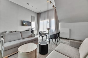 Uma sala de estar moderna com um sofá cinzento, uma mesa de centro redonda e um espaço de refeições com uma mesa de vidro e cadeiras.