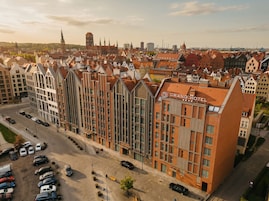 Um hotel moderno com uma placa visível, rodeado por arquitetura europeia tradicional.