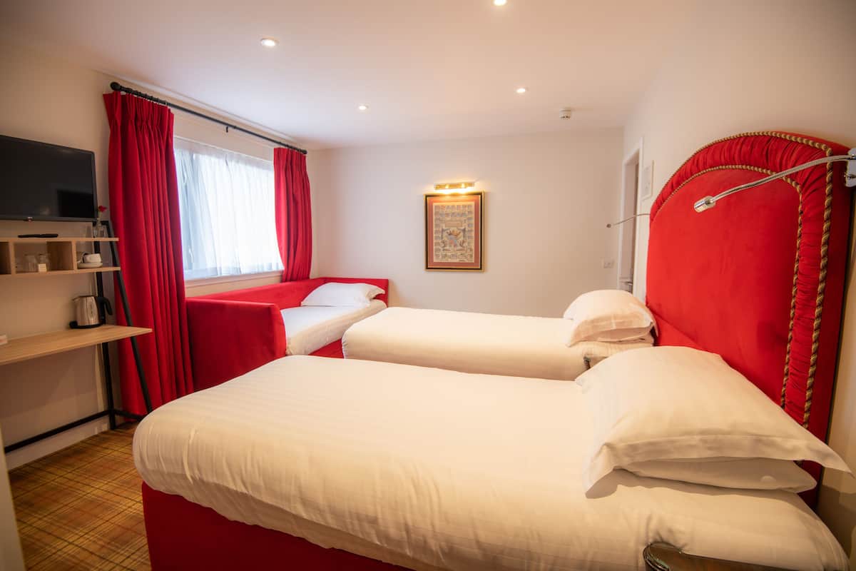 Quarto de hotel com duas camas, televisão, cortina vermelha e janela com cortinas translúcidas.