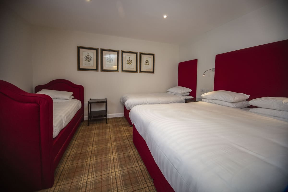 Quarto de hotel com duas camas de solteiro, cabeceira vermelha, mesa de cabeceira pequena e três quadros na parede.