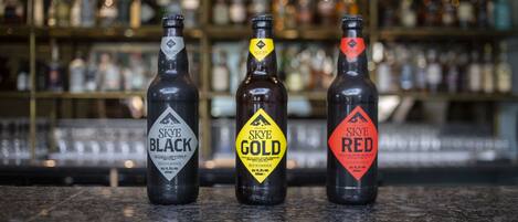Três garrafas de cerveja com as etiquetas 'Sky Black', 'Sky Gold' e 'Sky Red' em um balcão.