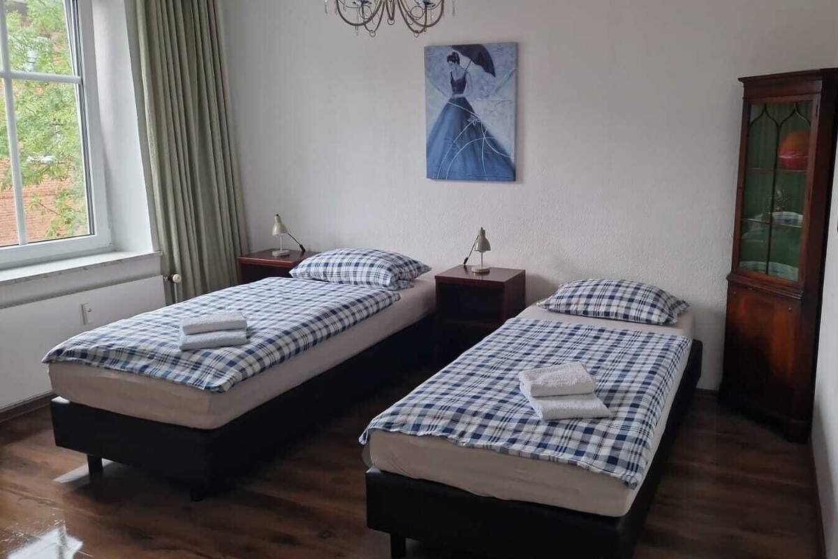 Quarto com duas camas, um quadro na parede, uma janela com cortinas e um armário de madeira.