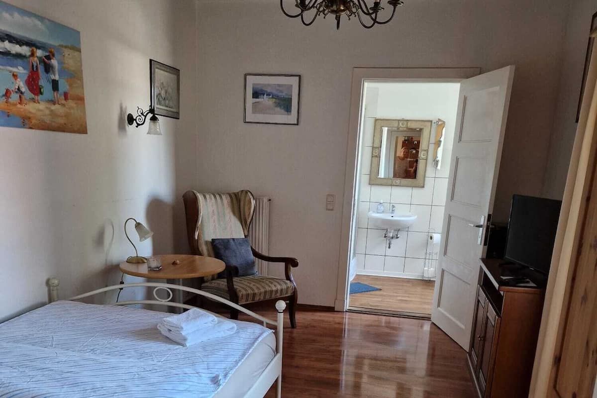 Quarto com cama, cadeira, mesa pequena e televisão.