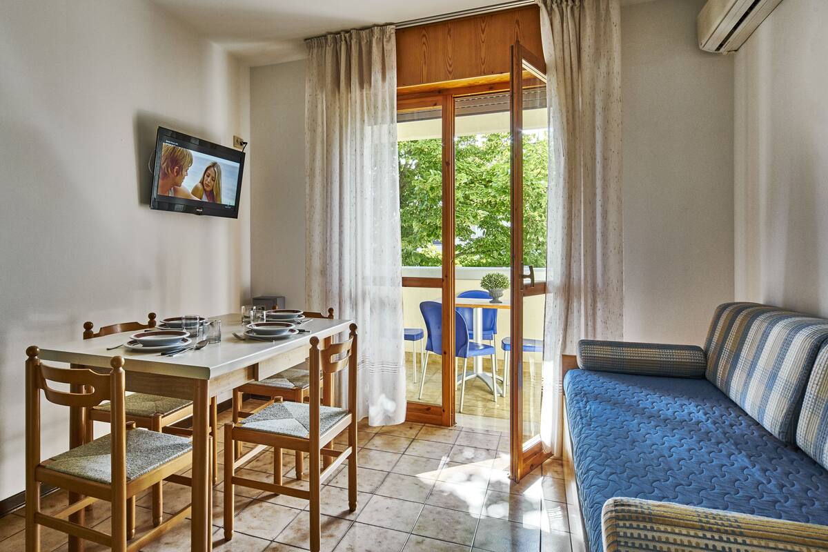 Uma área de refeições com mesa posta para quatro pessoas, cadeiras de madeira e um sofá azul.