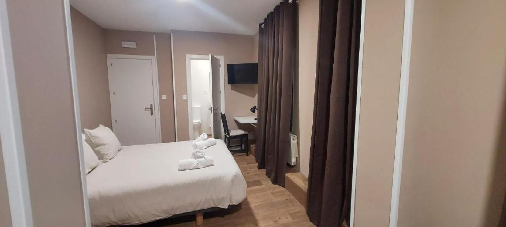 Quarto de hotel com cama, escrivaninha, cadeira e televisão.