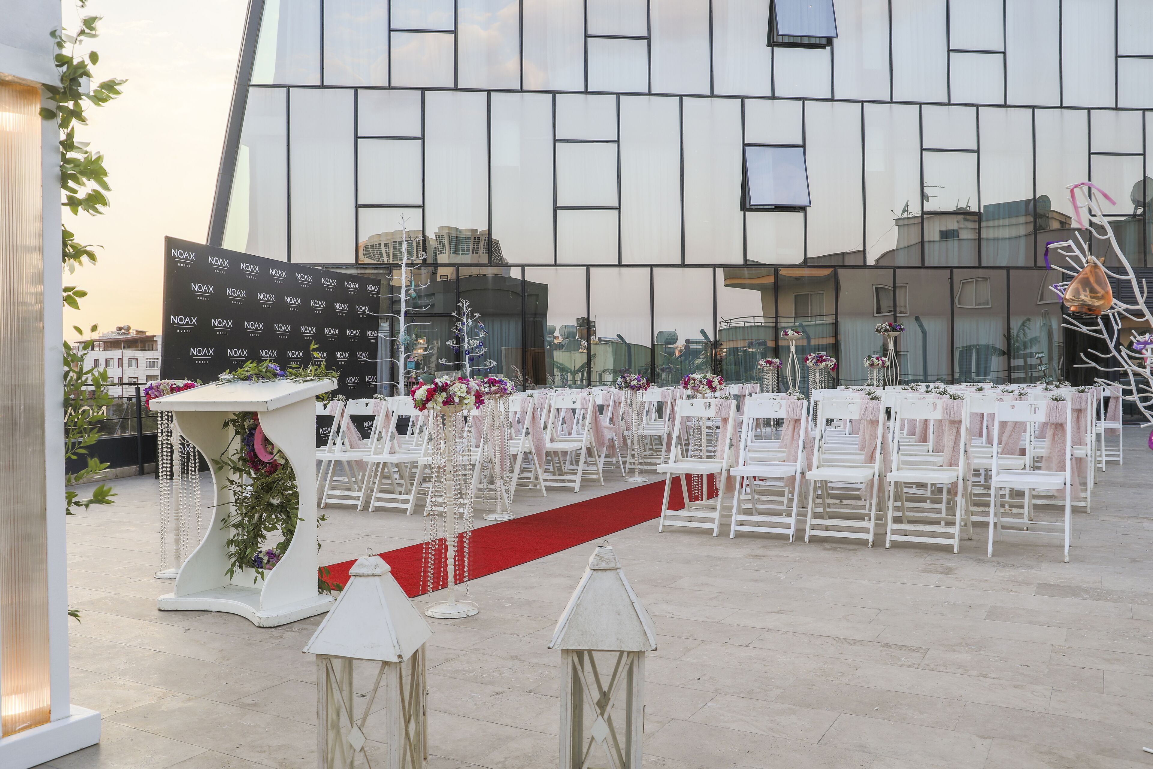 Decoração de casamento ao ar livre com cadeiras e mesas brancas, um tapete vermelho e detalhes florais.