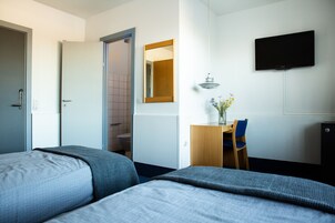 Quarto de hotel com duas camas, uma mesa de trabalho com cadeira, uma TV e um espelho.