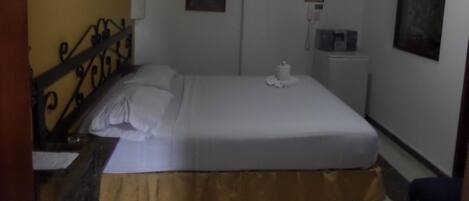 Quarto de hotel com cama, mesa de cabeceira, luminária, telefone e janela.