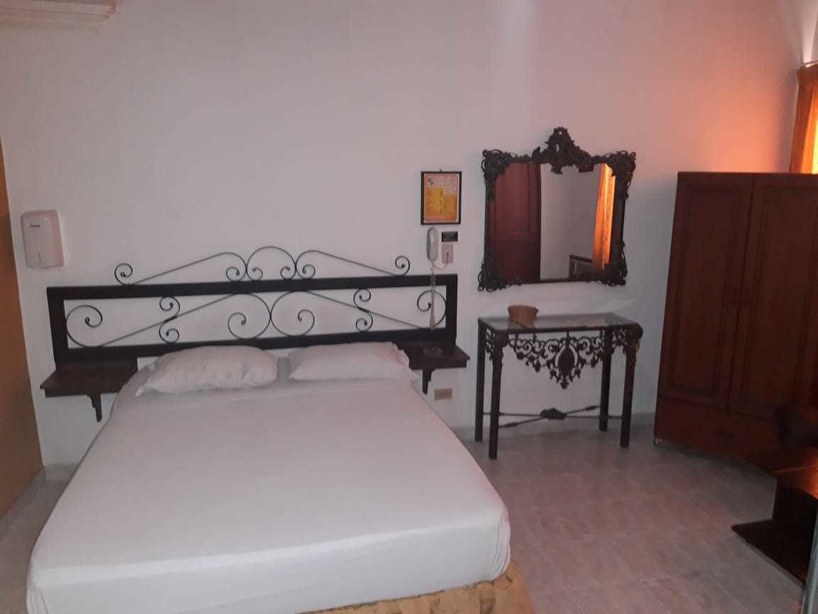 Um quarto com cama, mesa de cabeceira, espelho e guarda-roupa.