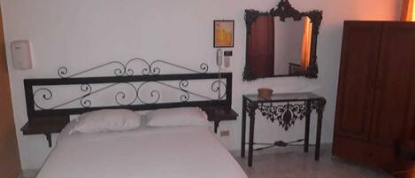 Um quarto com cama, mesa de cabeceira, espelho e guarda-roupa.