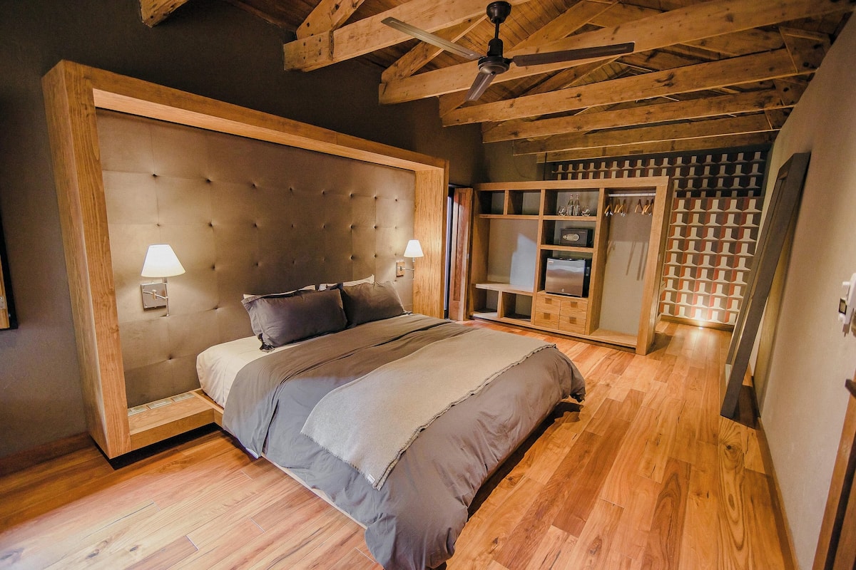 Quarto com cama grande, vigas de madeira no teto, guarda-roupa embutido e piso de madeira.
