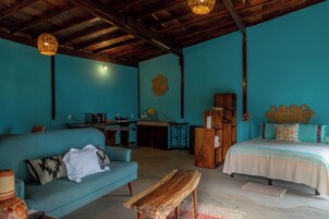 Quarto com sofá, cama, mesa de madeira, escrivaninha e luminária suspensa.