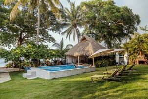 Piscina com um bangalô de palha e espreguiçadeiras.