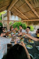 Um grupo de pessoas brindando com bebidas ao redor de uma mesa com comida e um laptop.