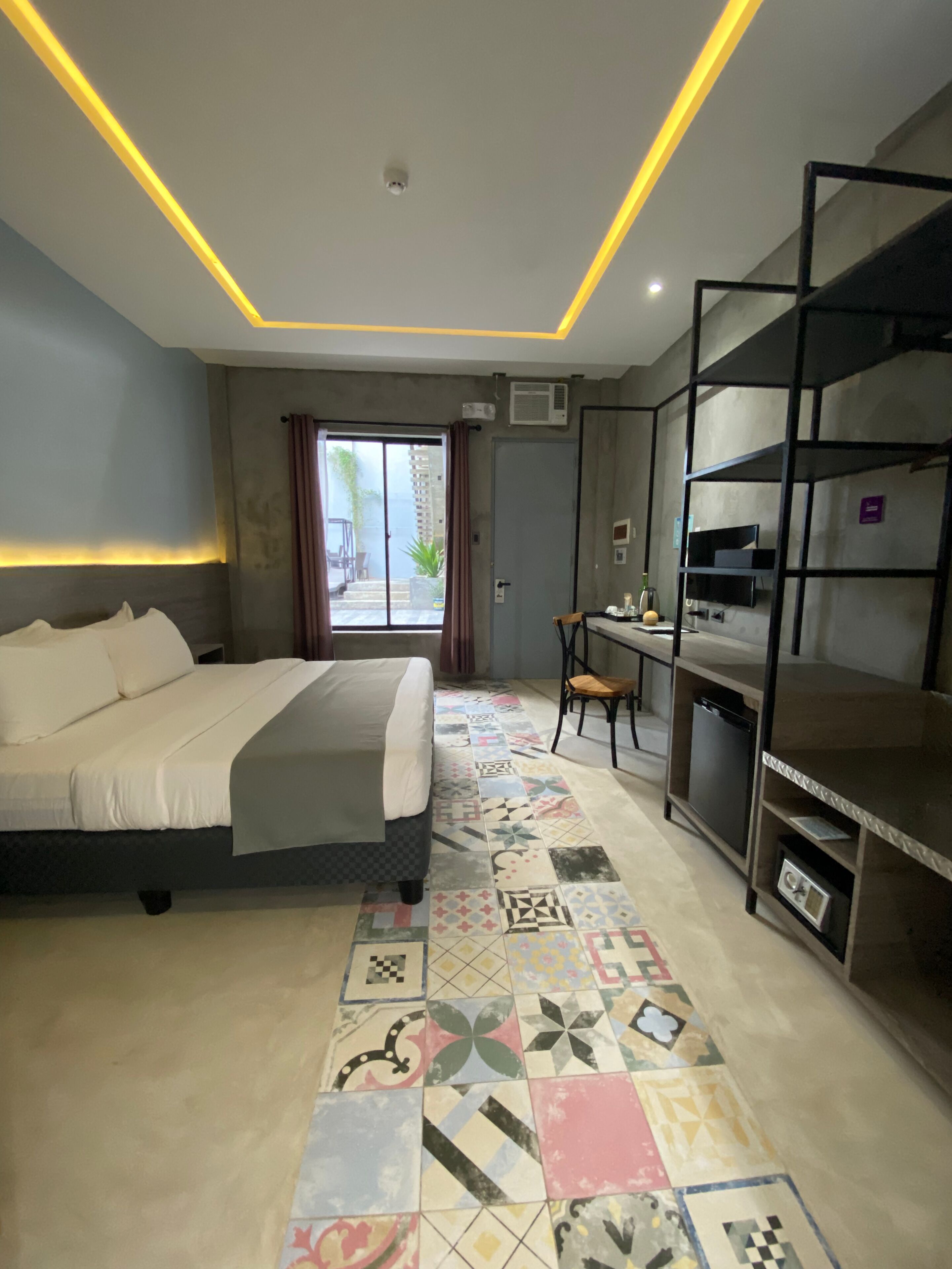 Quarto de hotel com cama, escrivaninha, cadeira e estantes embutidas.
