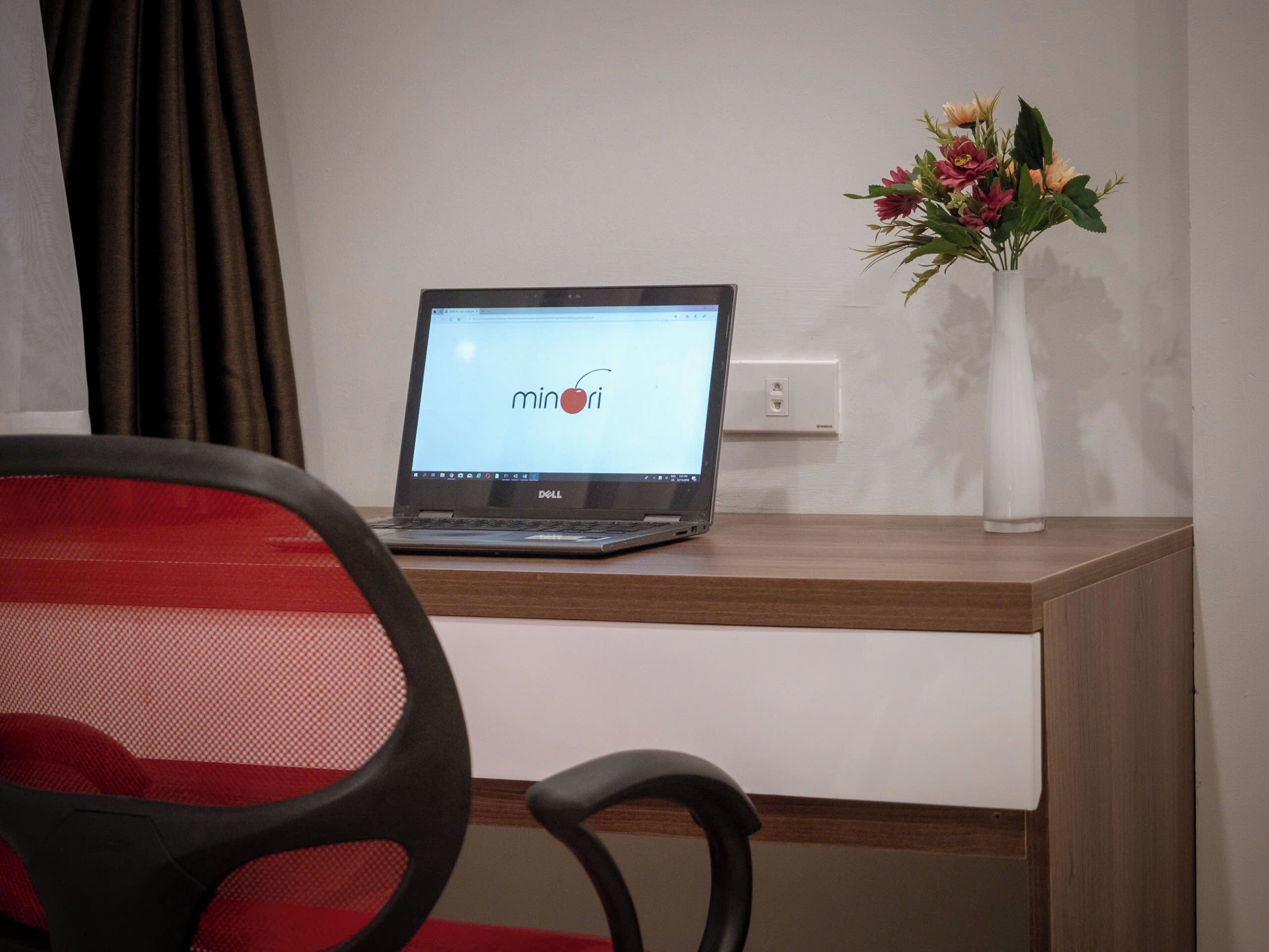 Um laptop numa mesa com um arranjo floral ao lado.