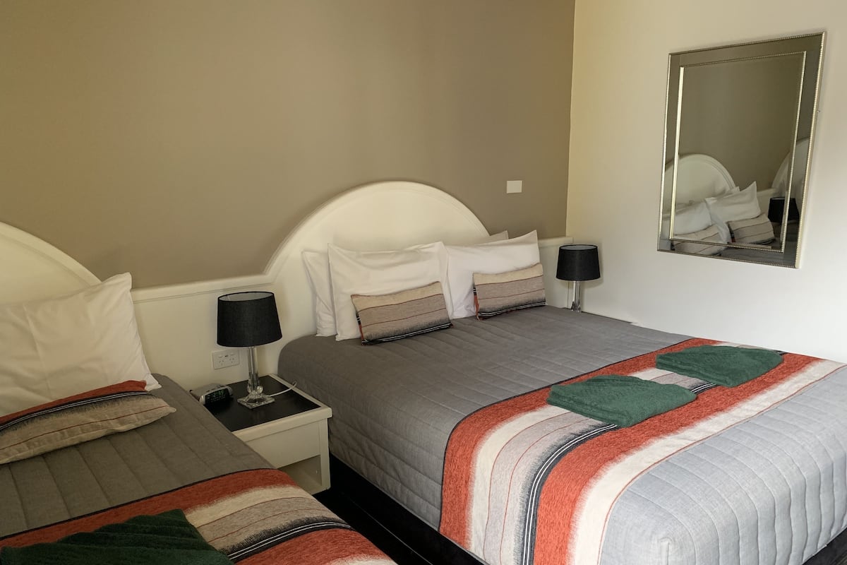 Quarto de hotel com duas camas, cada uma com cabeceira, mesas de cabeceira, luminárias e um espelho na parede.