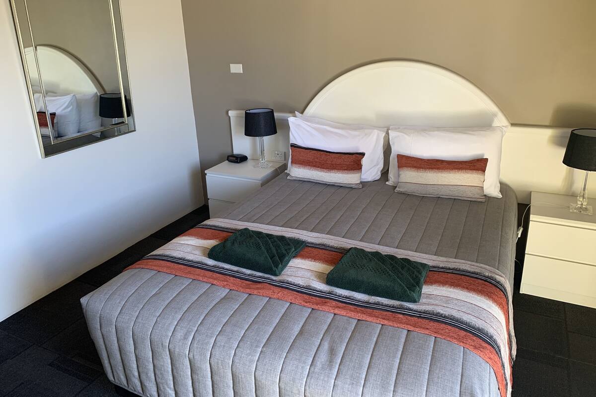 Quarto de hotel com cama, duas mesas de cabeceira, luminária e espelho.