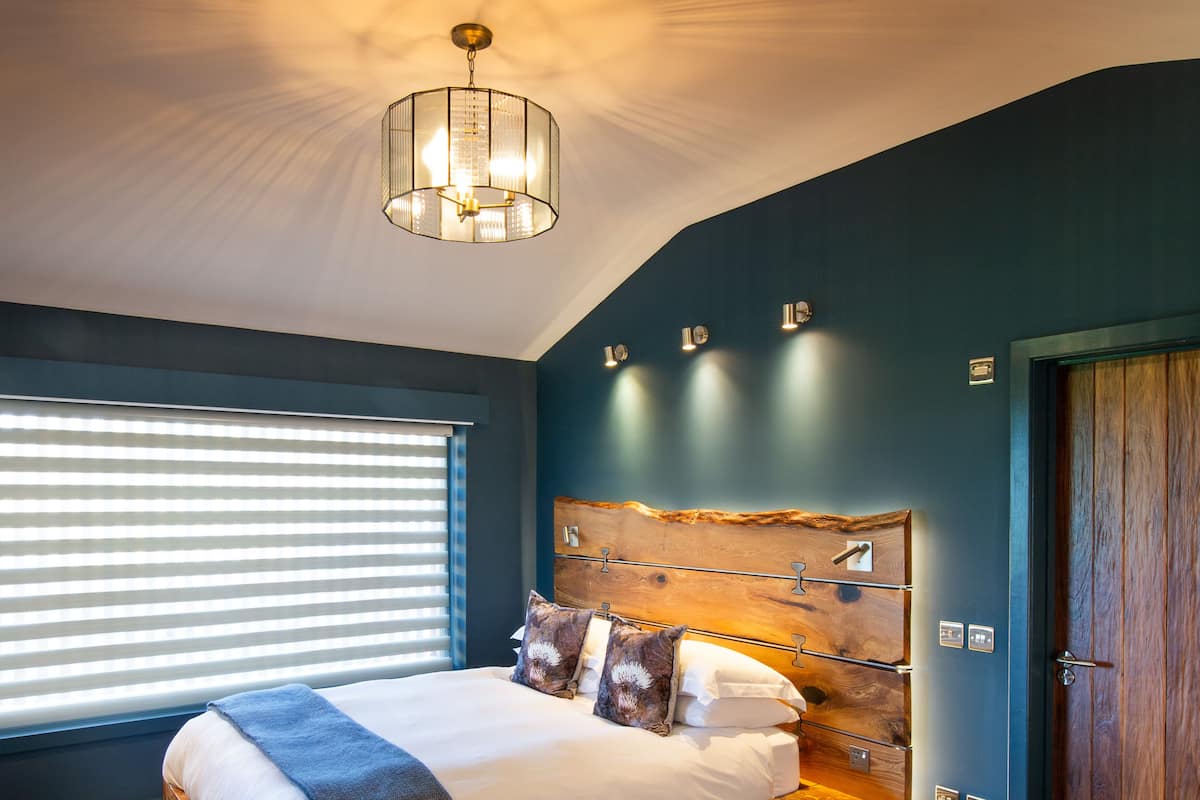 Quarto com cabeceira de madeira, cama grande com lençóis brancos, manta azul e tapete de couro.
