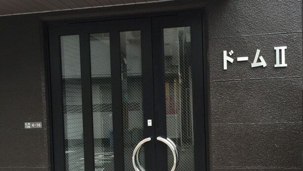 Um portão de metal preto com um puxador circular e uma placa em cima.