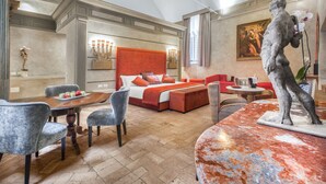 Um quarto amplo com uma cama grande, uma mesa de jantar com cadeiras e uma estátua.