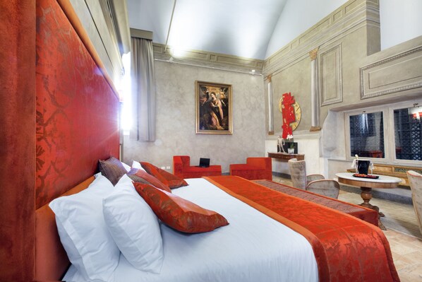 Quarto de hotel com uma cama grande, uma escrivaninha e uma cadeira. Há um quadro na parede e uma janela com vista.