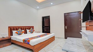 Quarto de hotel com uma cama, cabeceira de madeira, mesa de cabeceira, televisão fixada na parede e uma porta.