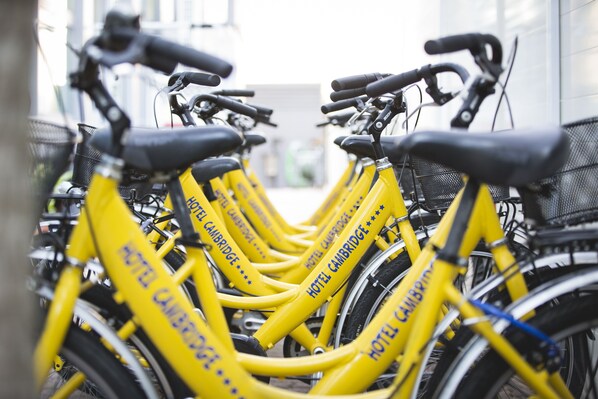 Uma fileira de bicicletas amarelas com a marca "HOTEL CAMBRIDGE", estacionadas em linha.