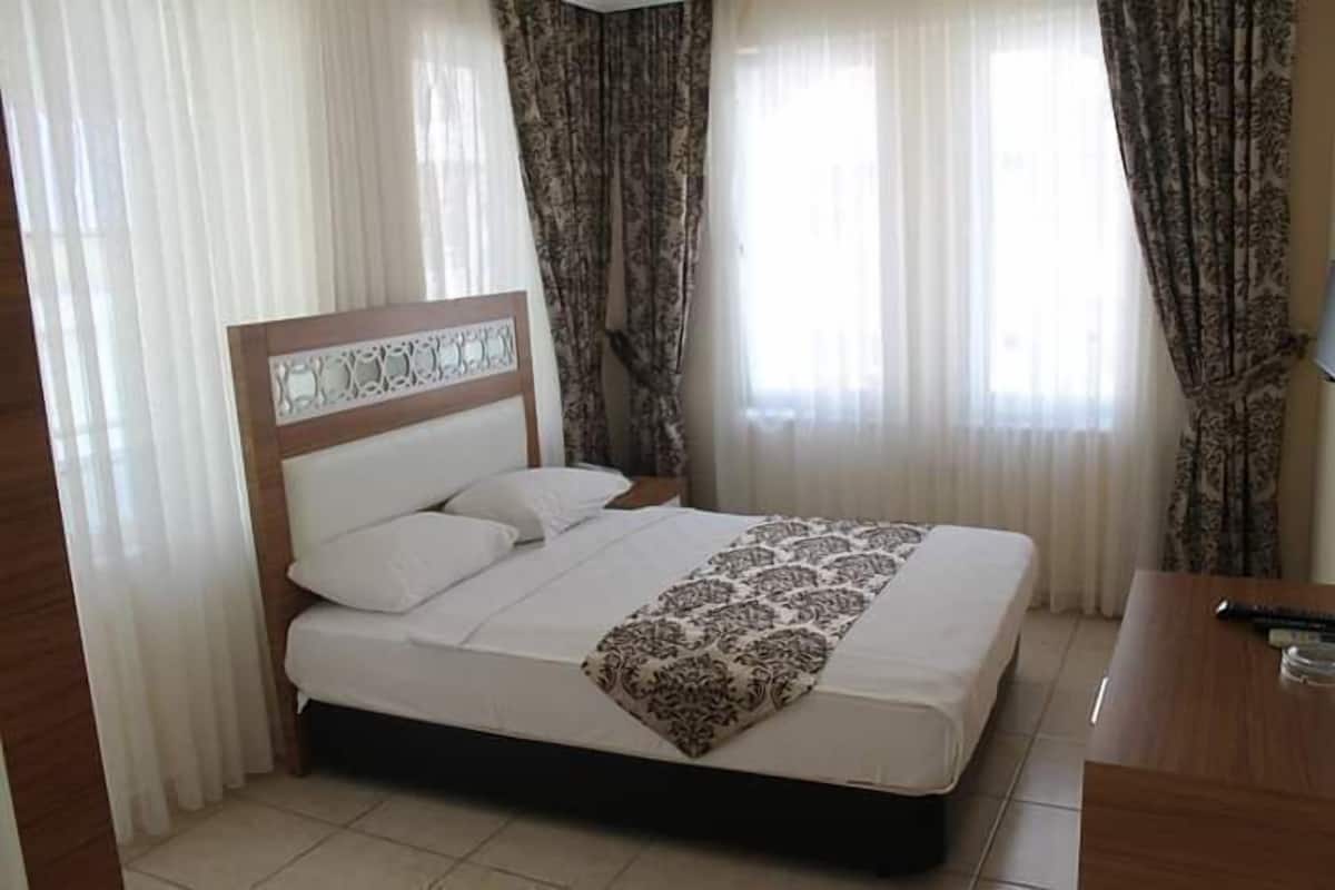 Uma cama bem arrumada com manta estampada, cabeceira de madeira e roupa de cama branca.