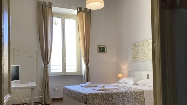 Quarto com cama, luminária de cabeceira e escrivaninha com computador.