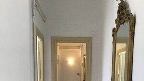 Um corredor com piso ladrilhado, um radiador e um espelho grande e ricamente decorado na parede.