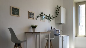 Uma cozinha moderna com bancada branca, dois bancos altos, uma mesa pequena e um vaso com planta.