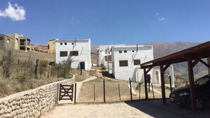 Conjunto de edifícios brancos com um muro de pedra e portão de madeira, com montanhas ao fundo.