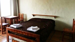 Quarto com cama de madeira, uma mesinha e duas cadeiras.