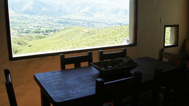 Uma área de refeições com uma grande janela que oferece vista para um vale e montanhas.