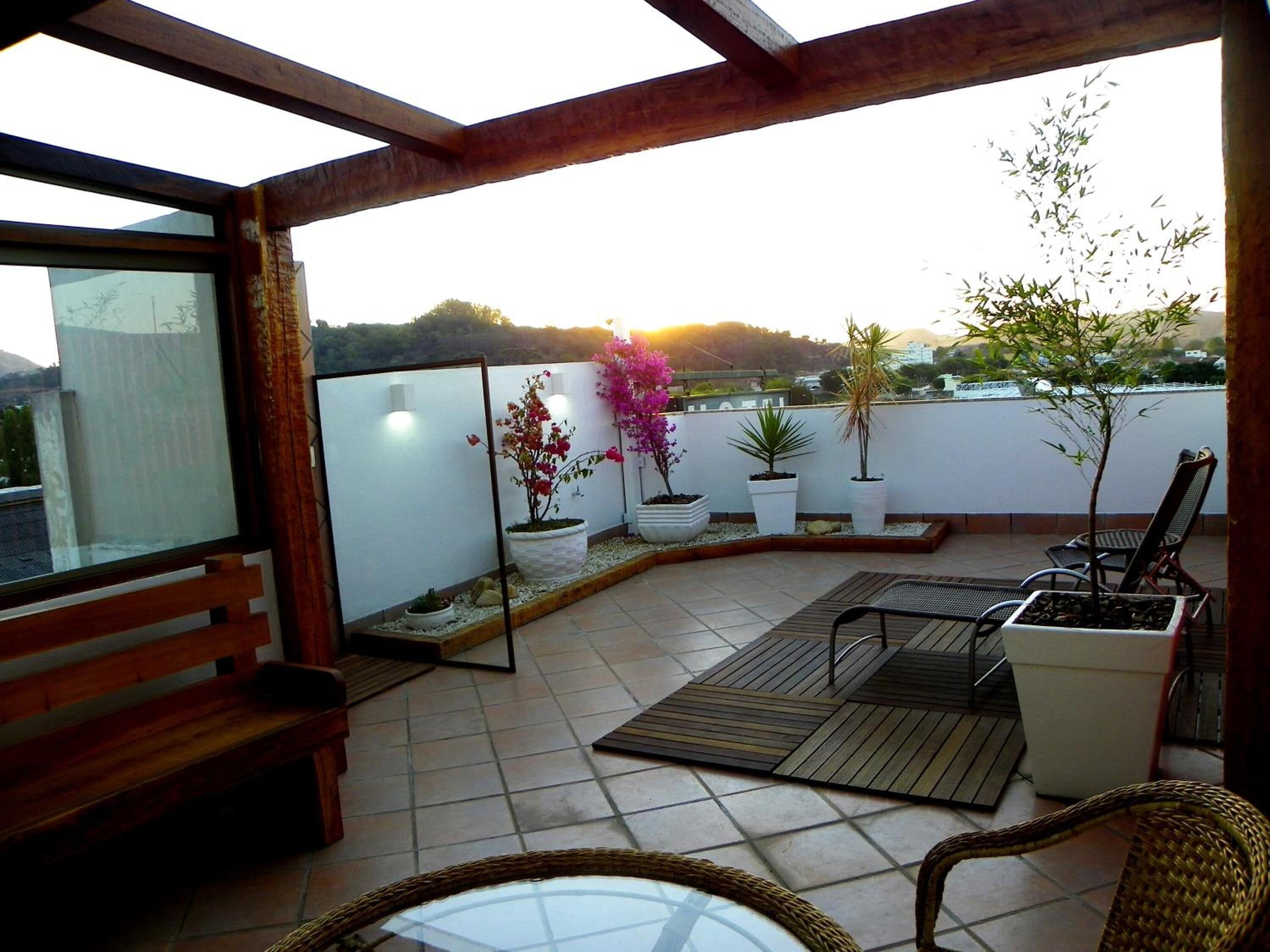 Terraço no telhado com um banco de madeira, duas cadeiras de vime e plantas em vasos.