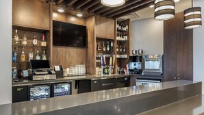 Uma área de bar com balcão, prateleiras com garrafas de bebidas, uma televisão e uma máquina de café.